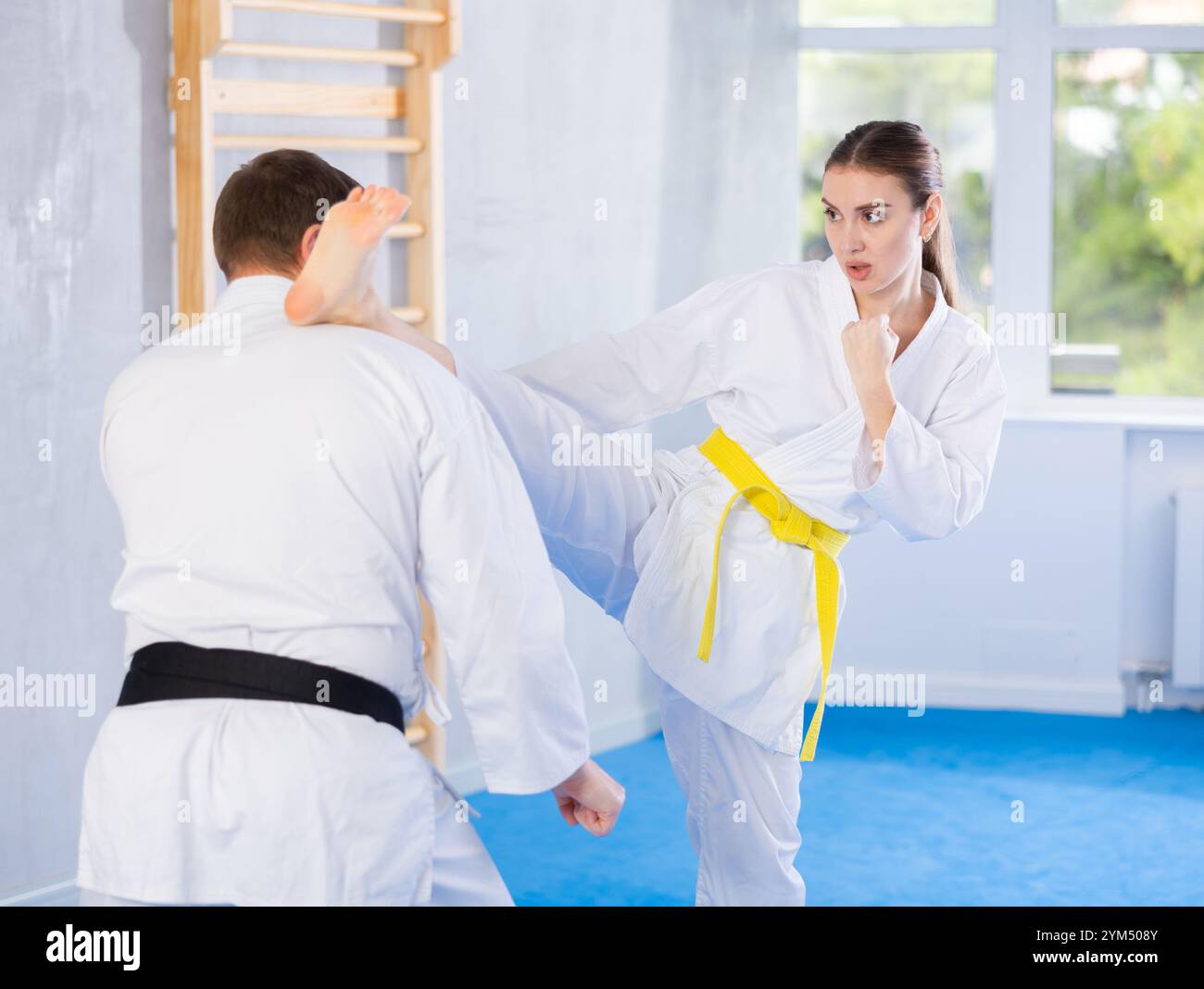 Young girl and middle-aged man practicing foot kicks and blocks in pair ...