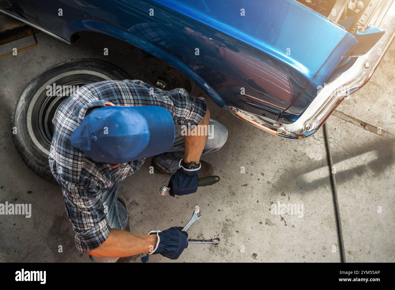 A mechanic focuses on repairing a classic car in a garage, surrounded ...