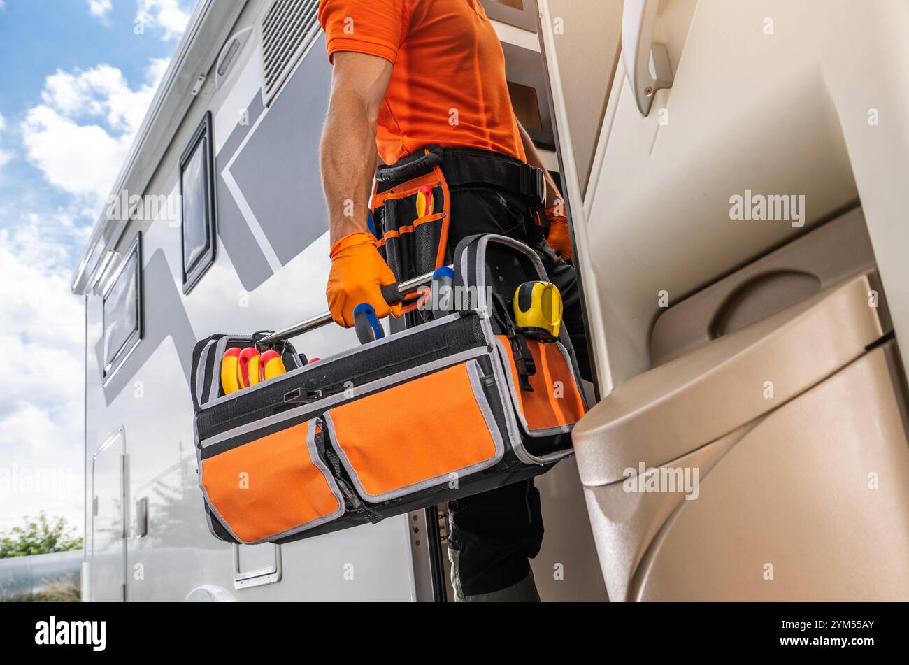 A technician dressed in orange is entering a recreational vehicle ...