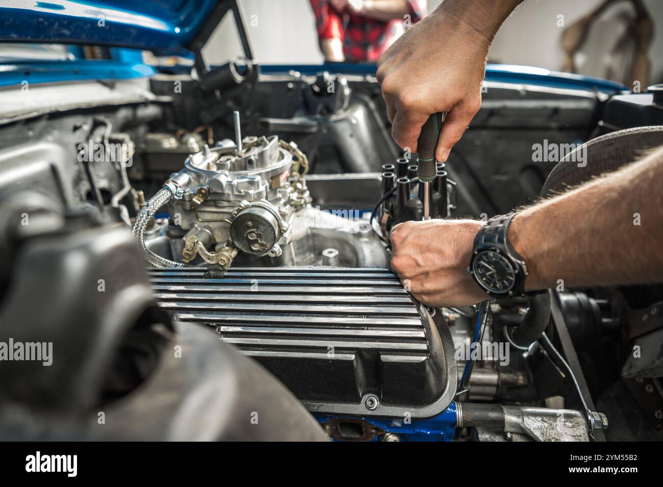 A person works on an engine inside a workshop, using tools to tighten ...