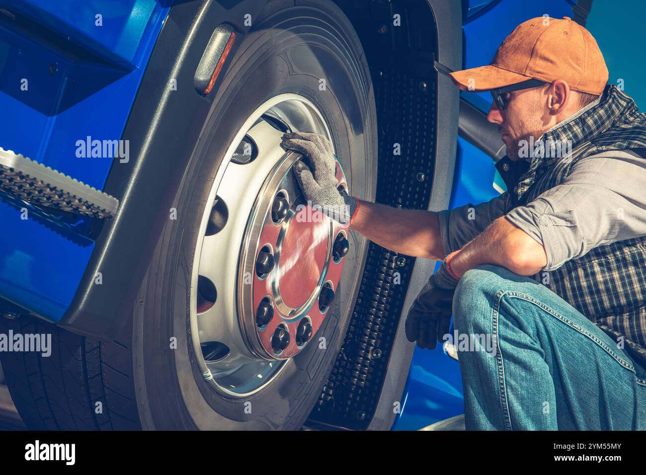 A mechanic kneels beside a blue semi truck, carefully checking the tire ...