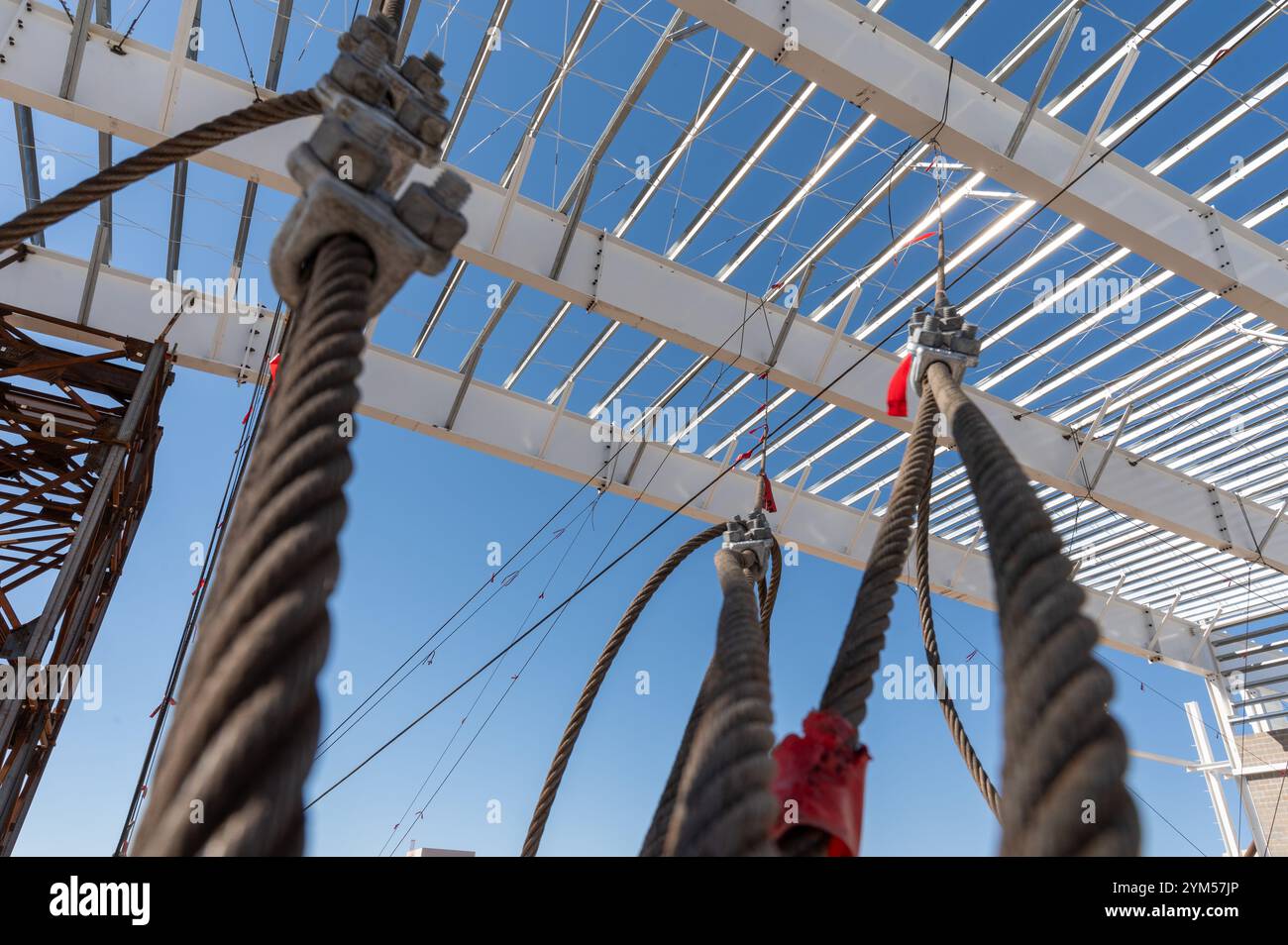 Steel wire ropes extend from the base of an aircraft hangar to the metal truss assemblies on the ...