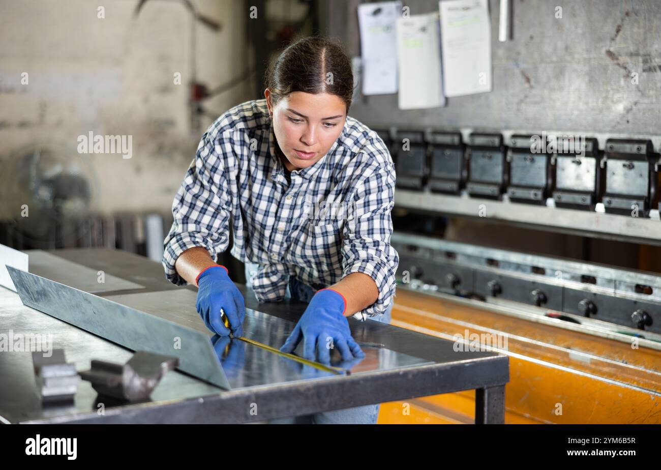 Workwoman measuring steel sheet with tape measure in metal workshop ...