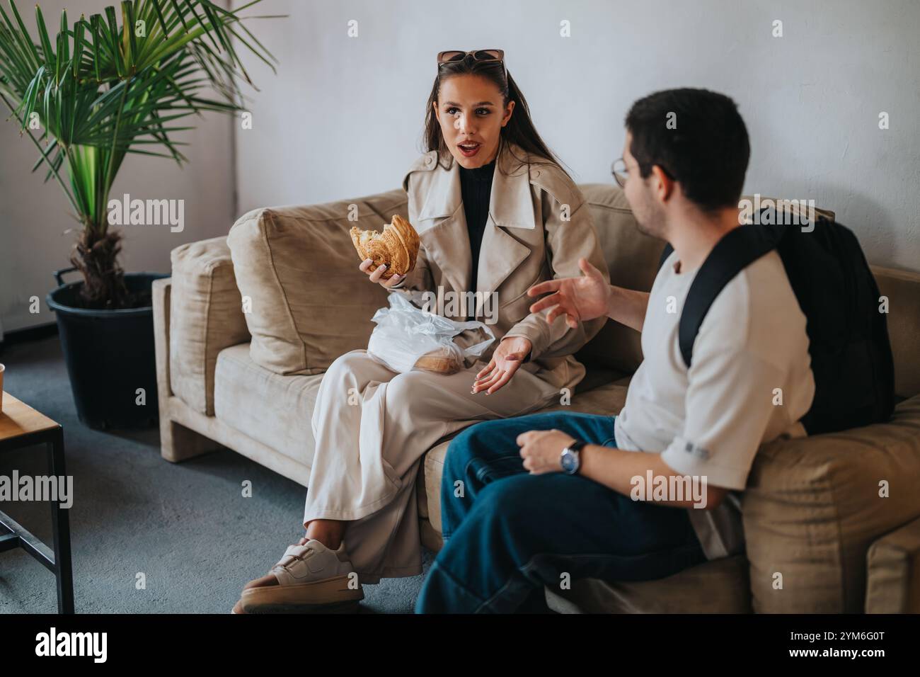 Two students share a casual breakfast on a couch, engaged in friendly ...