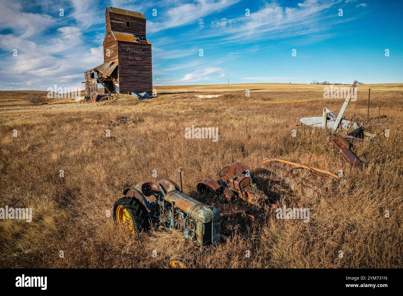 An old tractor is laying in a field next to a grain silo. The tractor ...