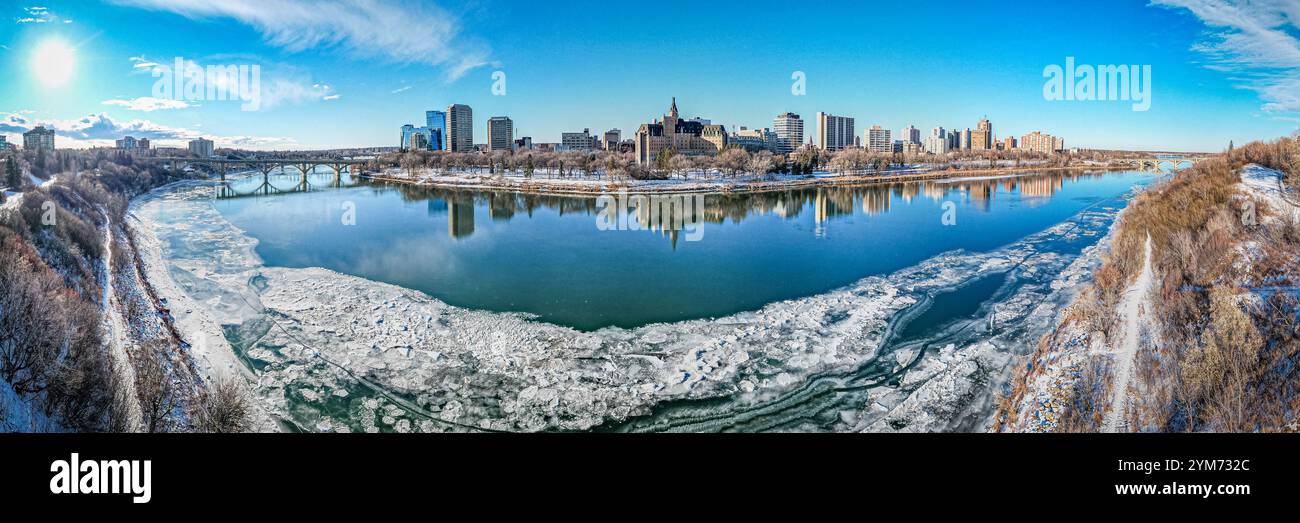 A city skyline of Saskatoon is reflected in the water. The sky is blue ...