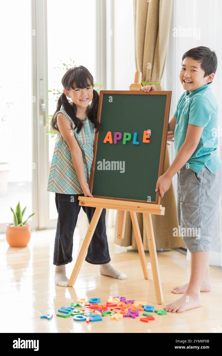 Brother and sister standing next to blackboard with alphabet table ...