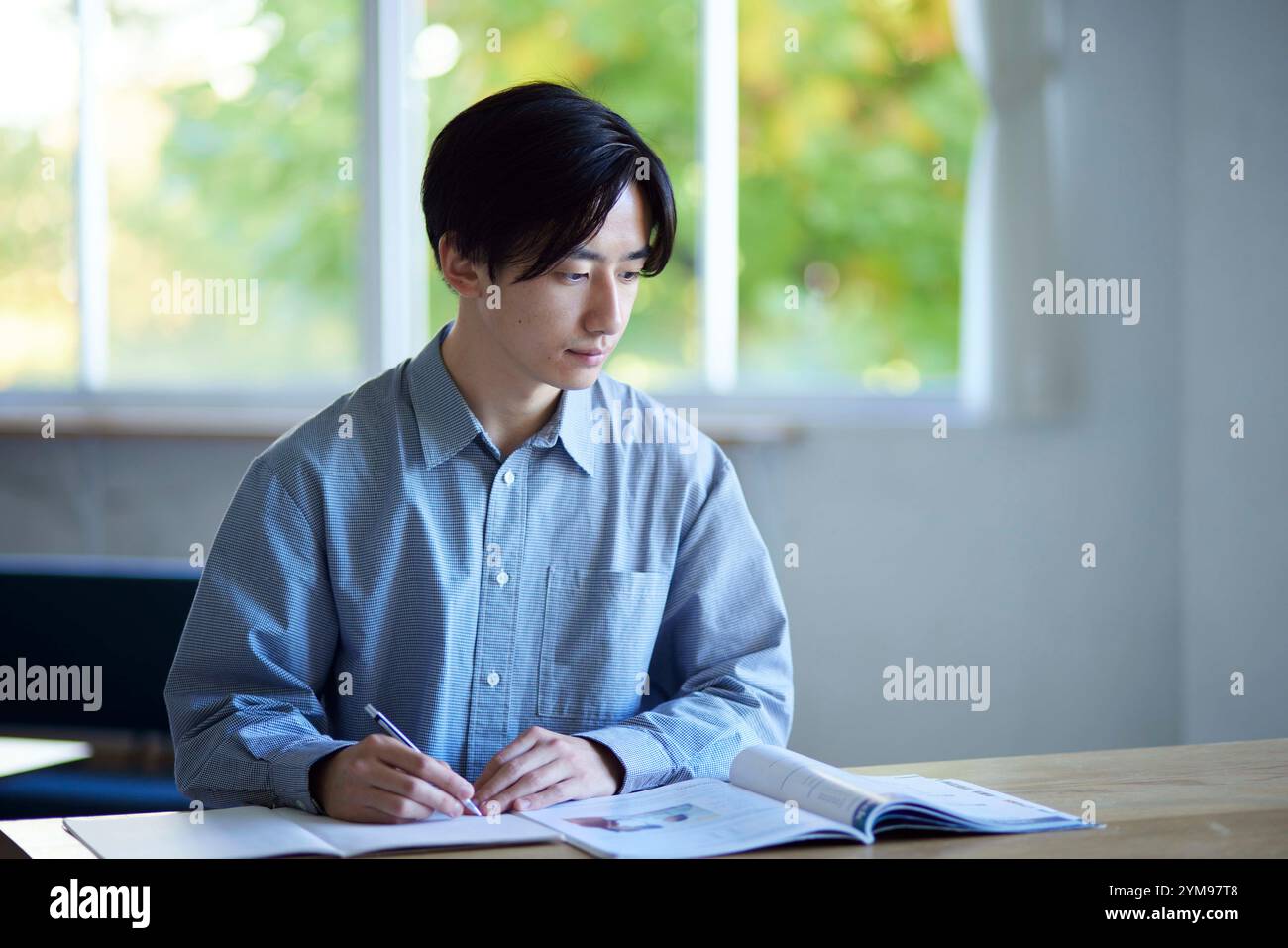 A male Japanese university student studying in the living room of his ...