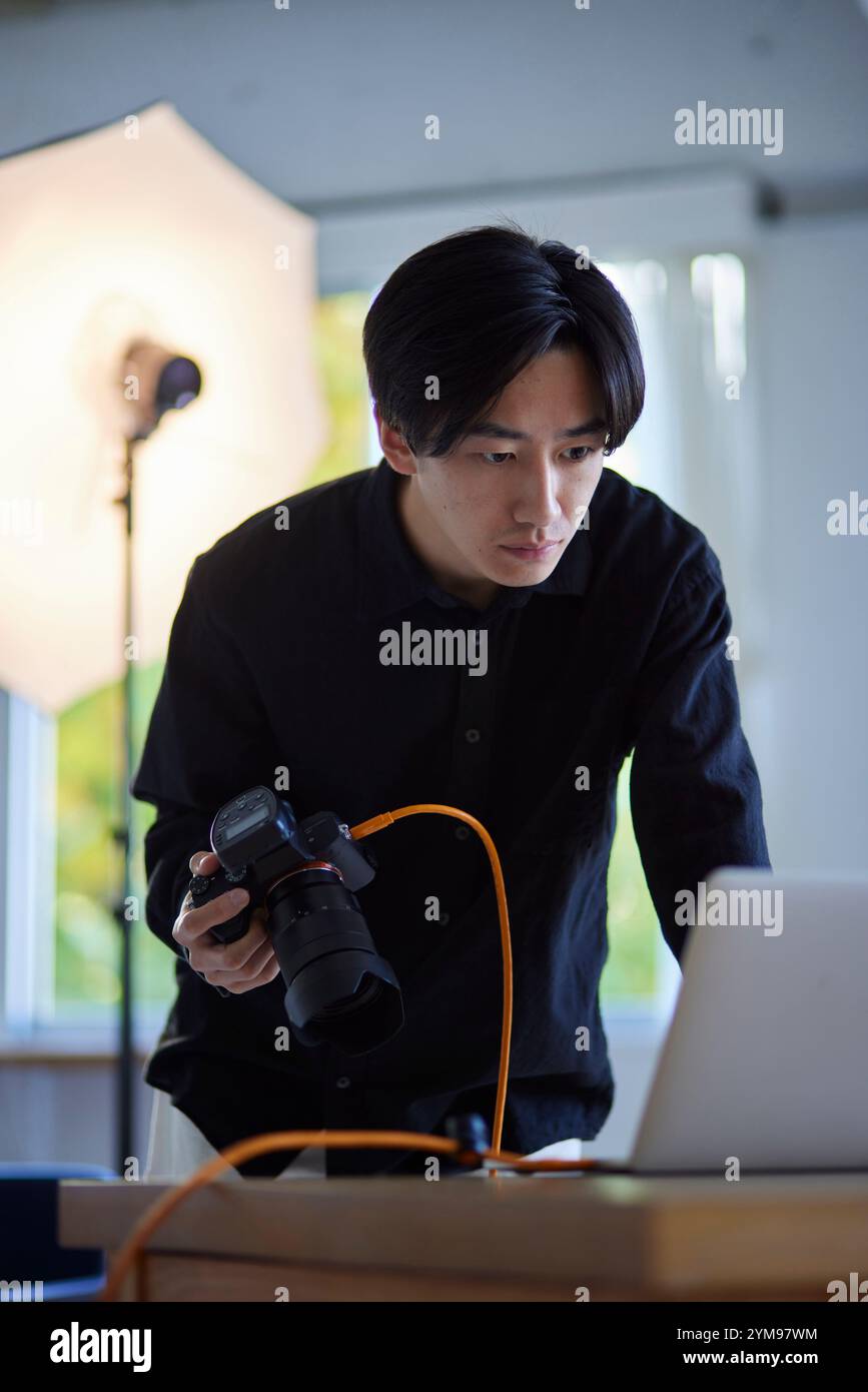 A Japanese male photographer operating a laptop computer in a photo ...