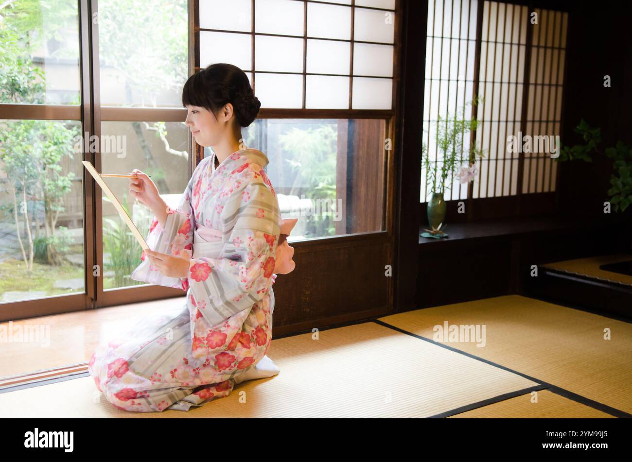 Woman in kimono sitting seiza and writing haiku on a tanzaku strip of ...