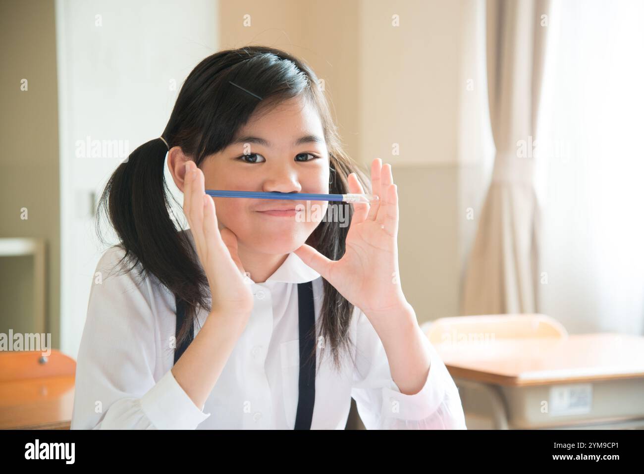 Primary school girl holding pencil and laughing Stock Photo - Alamy