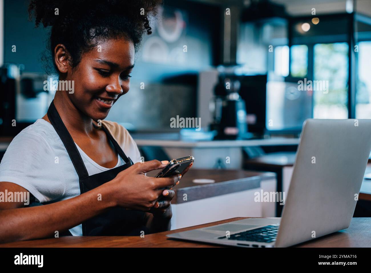 Coffee shop owner a focused black woman in apron using smartphone in ...