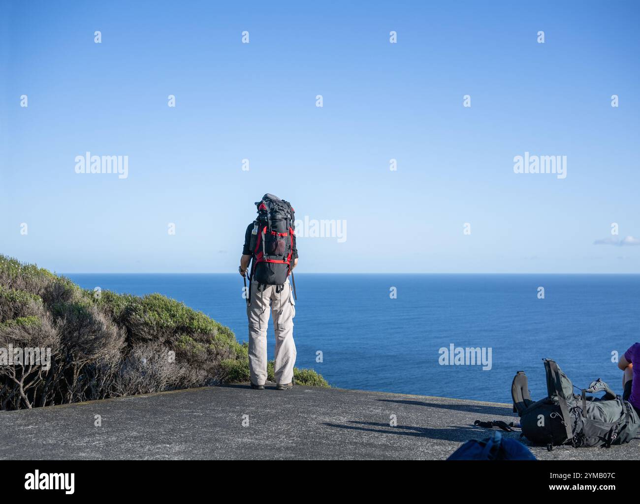Backpacker looking at the ocean at Cape Brett Track. Backpacks lying on ...