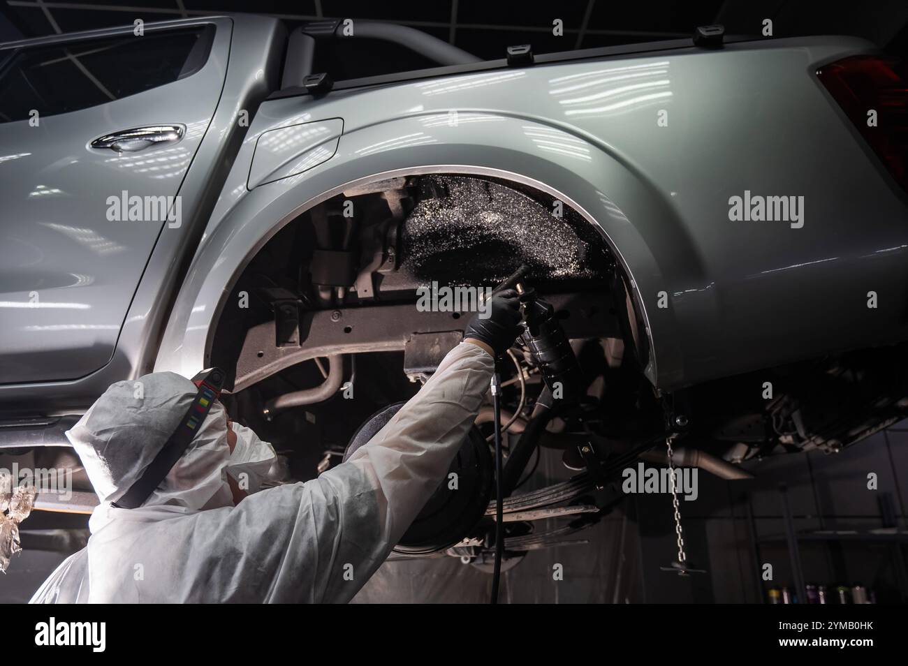 An auto mechanic applies anti-corrosion mastic to the underbody of a ...