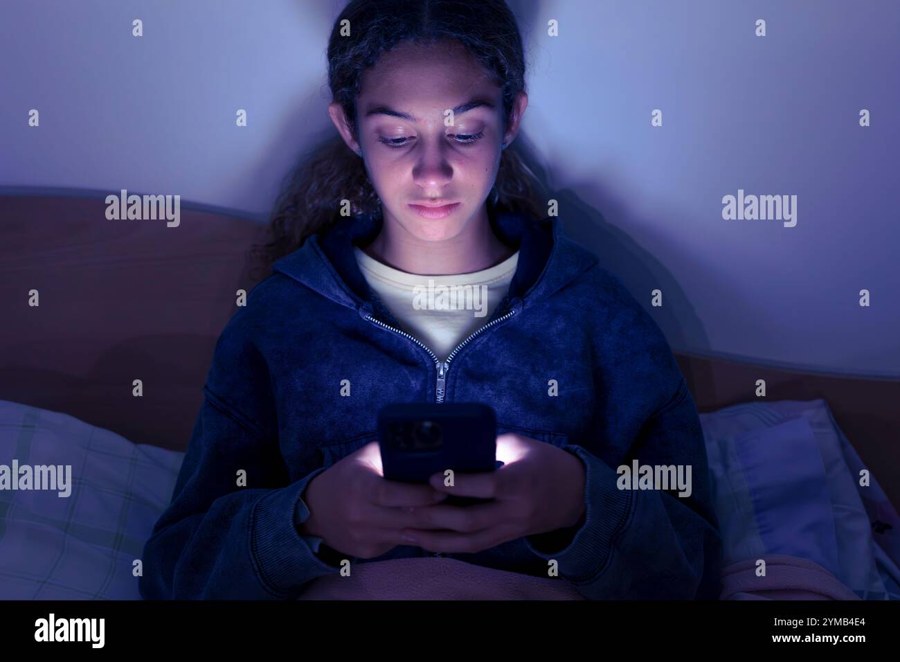 Sad and tired teenager girl using a smartphone lying in bed late at ...