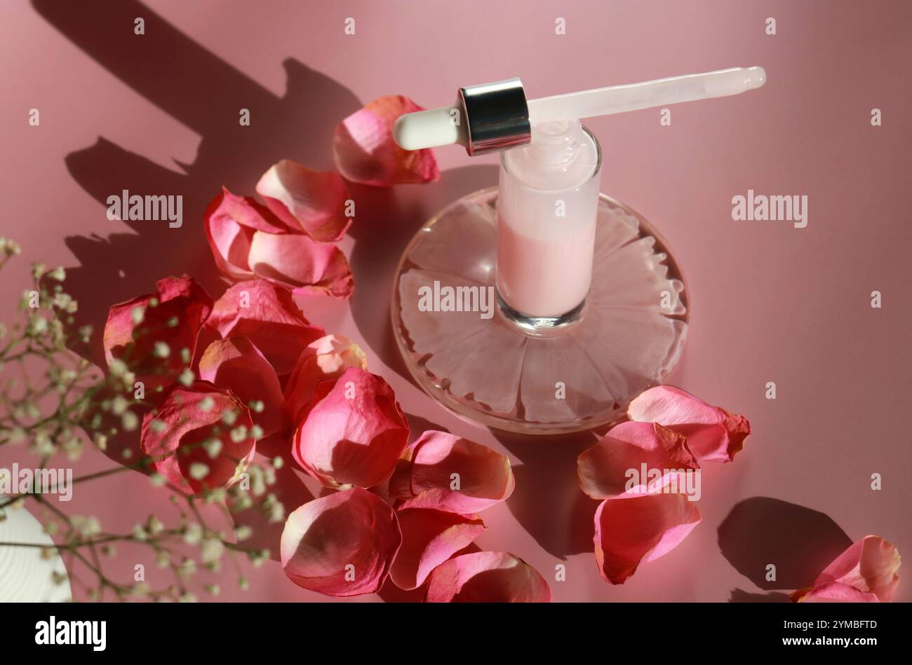 A bottle of facial serum lotion with roses extract on pink background ...
