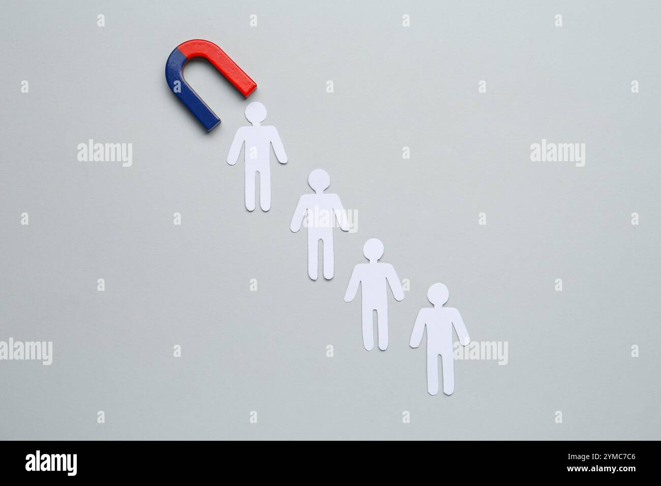 Magnet attracting paper cutouts of humans on light grey background ...