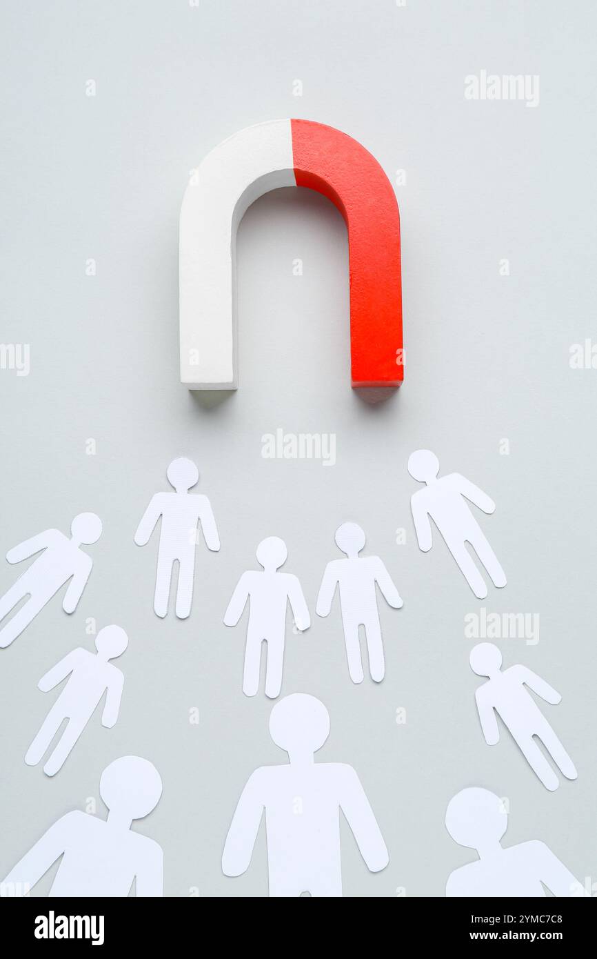 Magnet attracting paper cutouts of humans on light grey background ...