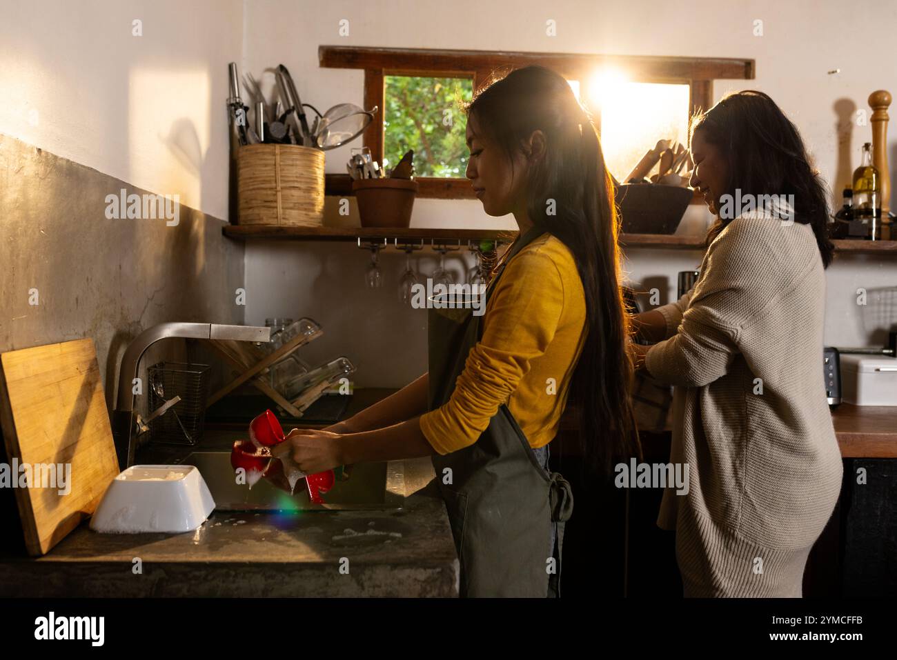 asian female teenager washing dishes while grandmother prepares meal in ...