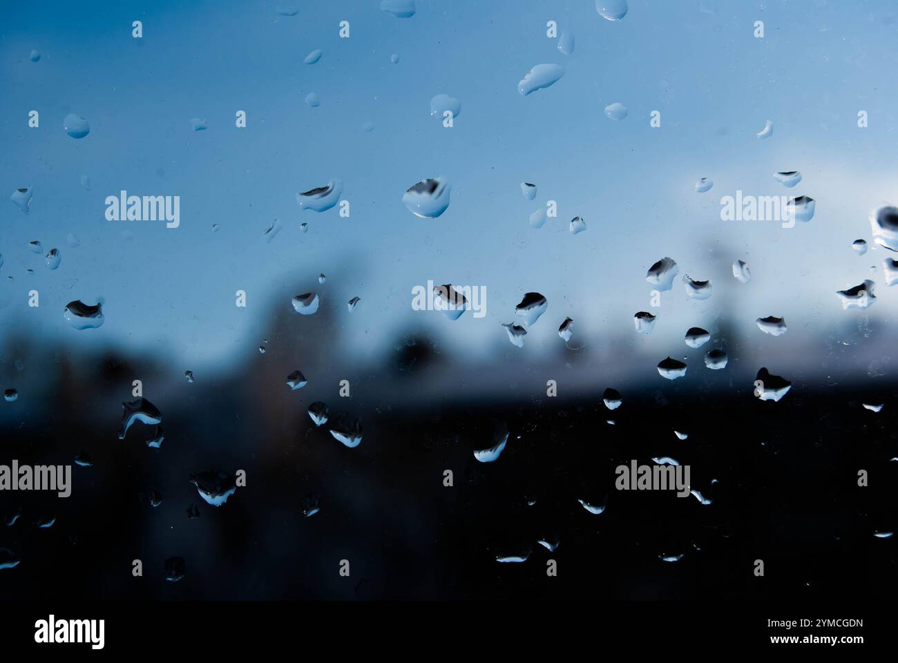 Clear water droplets scattered on a glass window, reflecting light and creating a textured ...