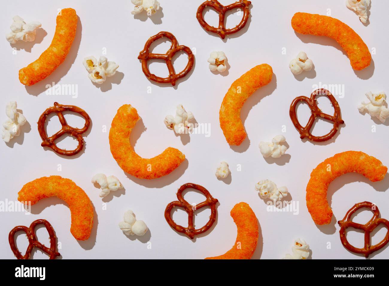Overhead view of pretzels, cheese puffs and popcorn on white background ...