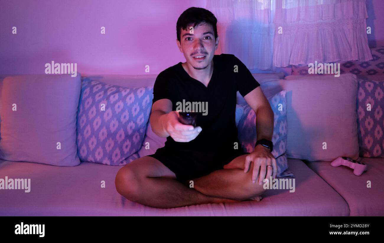 Young man sitting with his feet up on the couch watching television flipping through channels ...