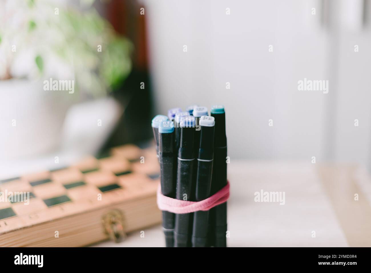 A box of pens is on a table next to a chess board. The pens are black ...