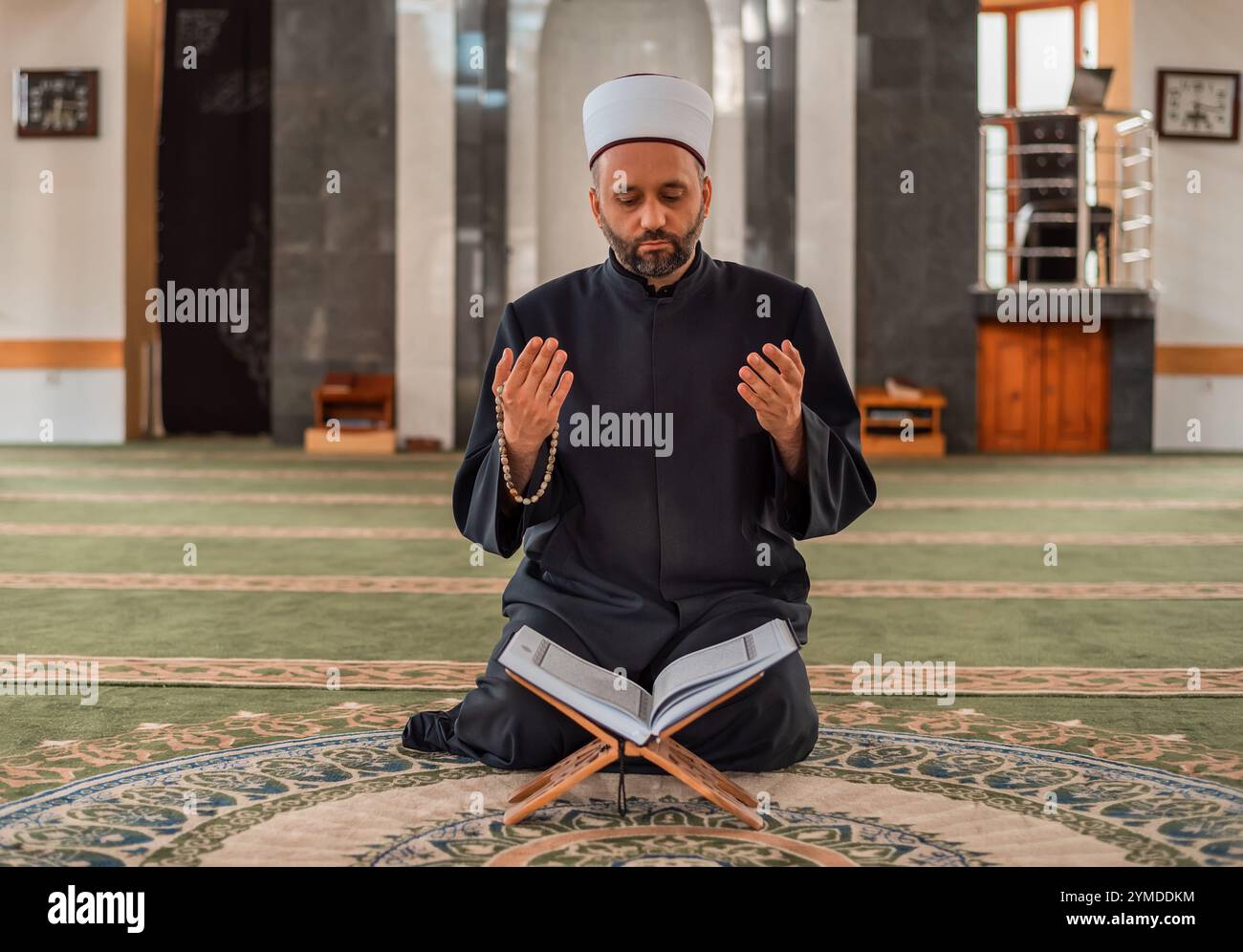 A Muslim prayer man praying with hands up while reading a Quran inside ...