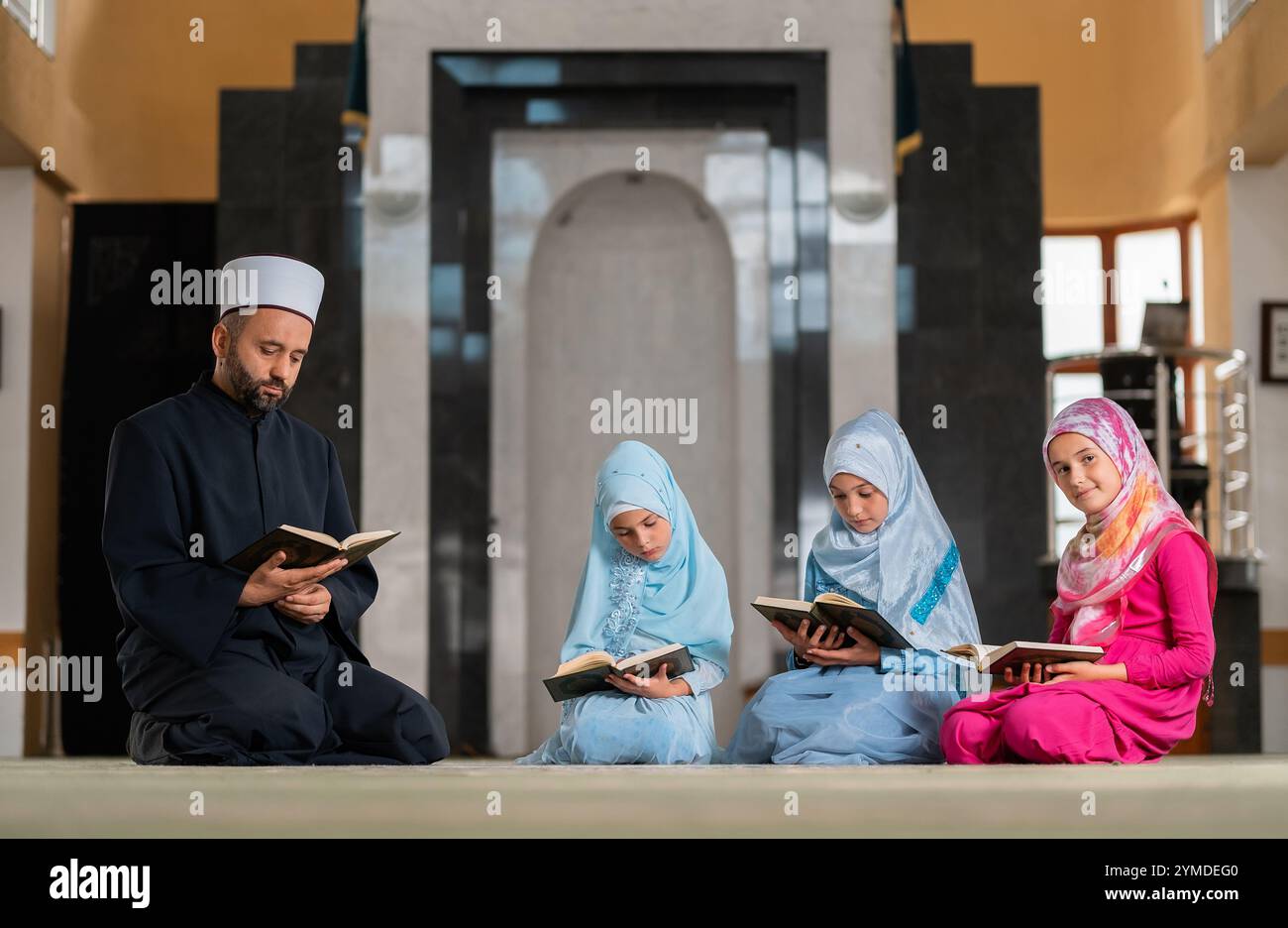 A Muslim teacher teaches children girls to read a holy book Quran inside the Mosque group of ...
