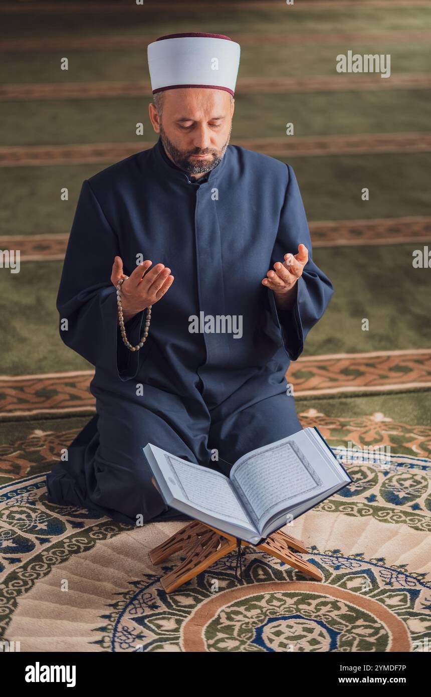 A Muslim prayer man praying with hands up while reading a Quran inside ...