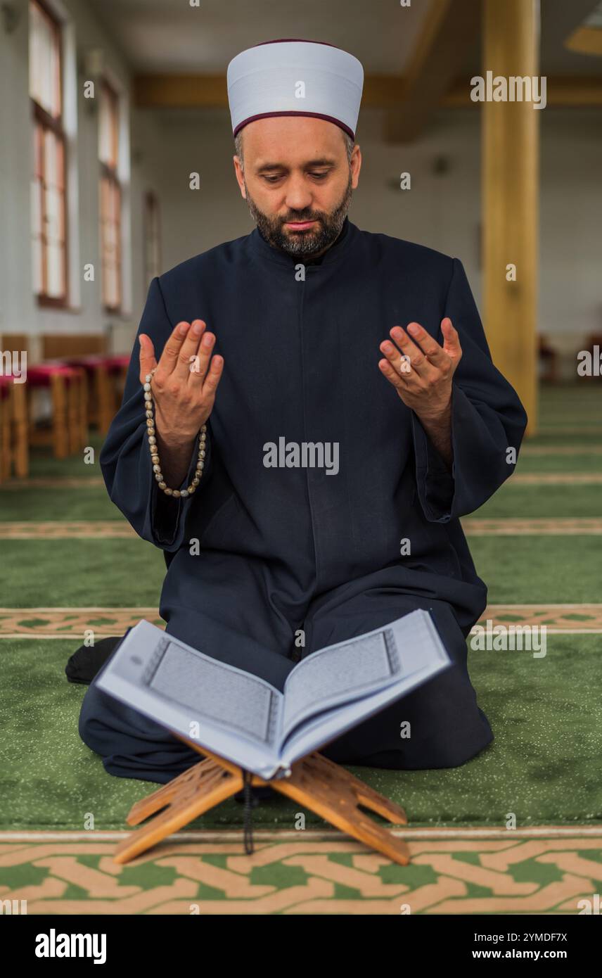 A Muslim prayer man praying with hands up while reading a Quran inside ...