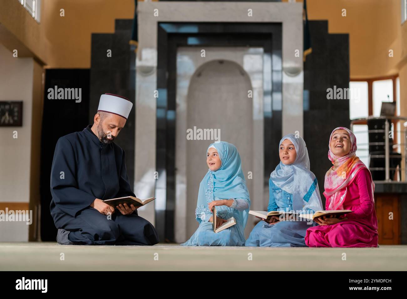 A Muslim teacher teaches children girls to read a holy book Quran inside the Mosque group of ...