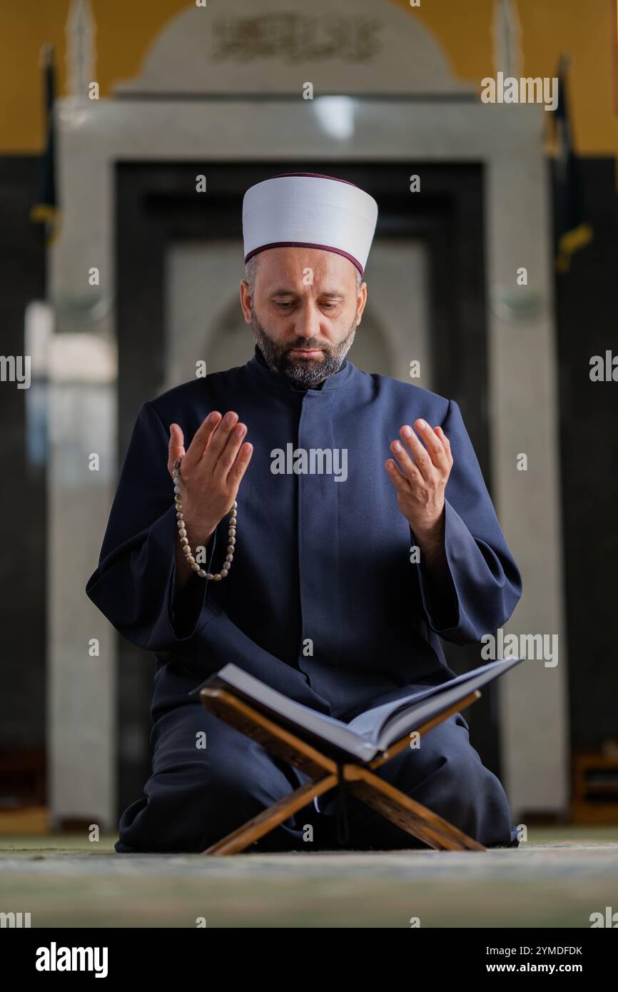 A Muslim prayer man praying with hands up while reading a Quran inside ...