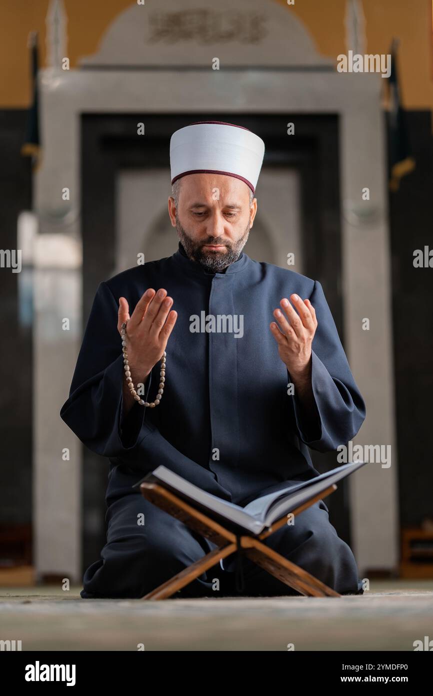 A Muslim prayer man praying with hands up while reading a Quran inside ...