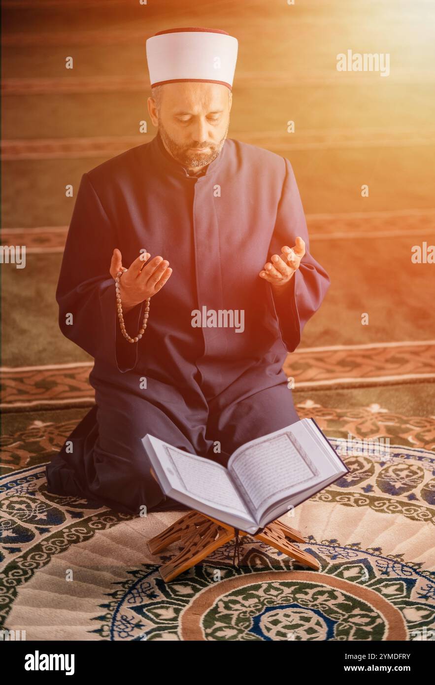 A Muslim prayer man praying with hands up while reading a Quran inside ...
