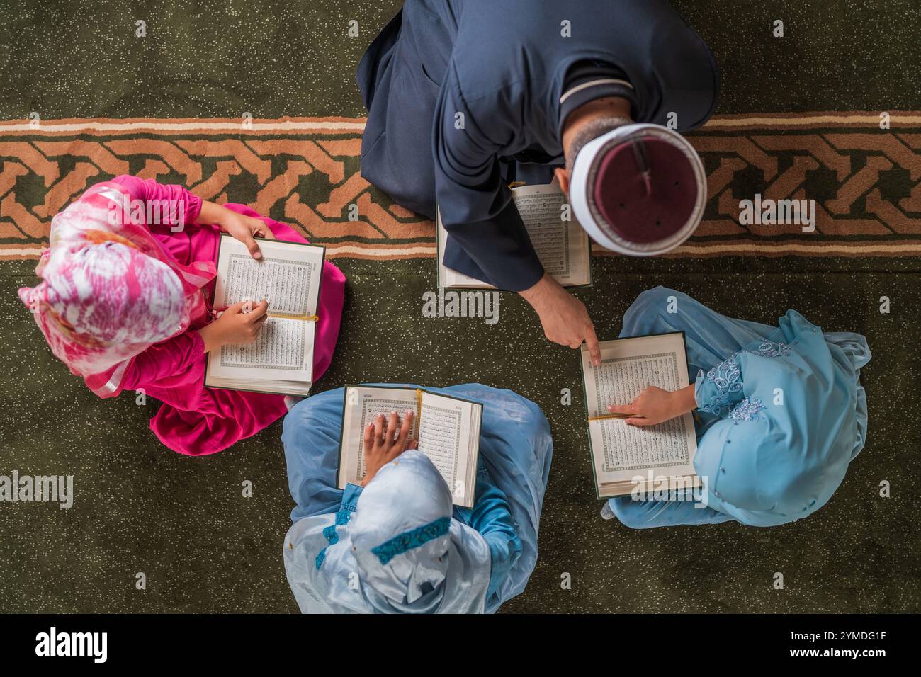 A Muslim teacher teaches children girls to read a holy book Quran ...