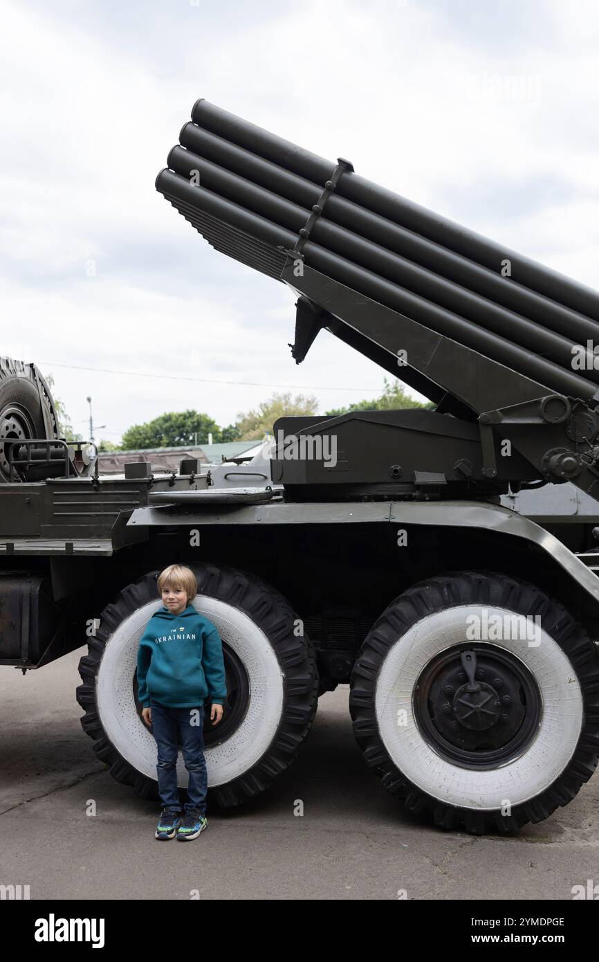 young boy stands near military vehicle, multiple launch rocket system ...