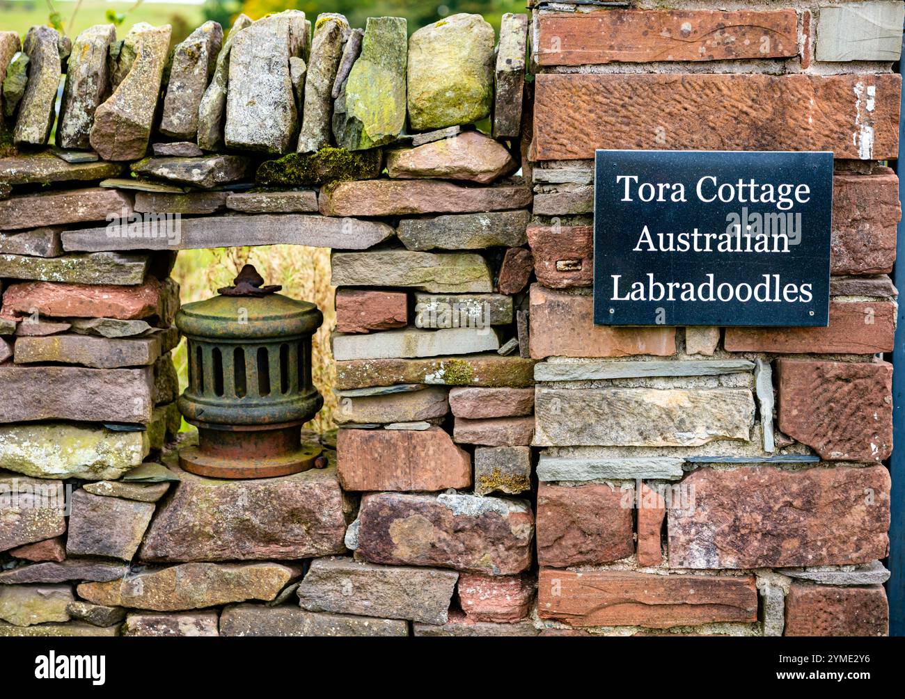 A black sign with white text is mounted on a rustic stone wall ...