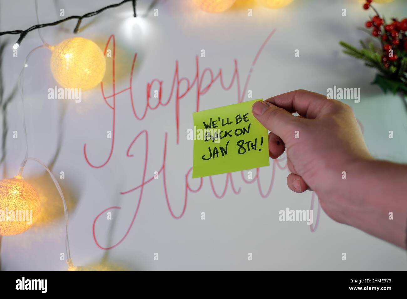 Hand holding yellow sticky note with return date message against white ...