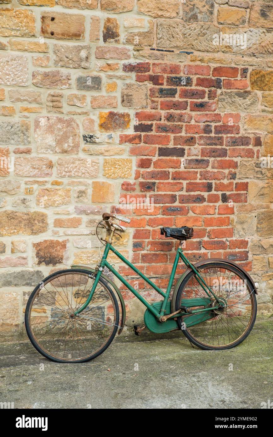 A green and rusty abandoned bicycle leaning against the wall of a ...