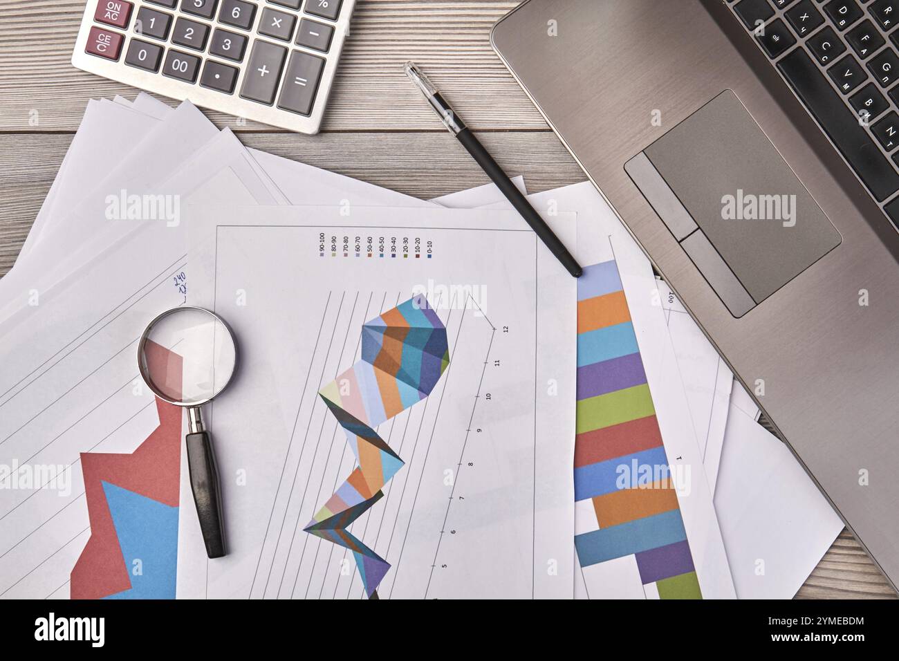 Papers with charts and glass magnifier with pen. Laptop device with ...