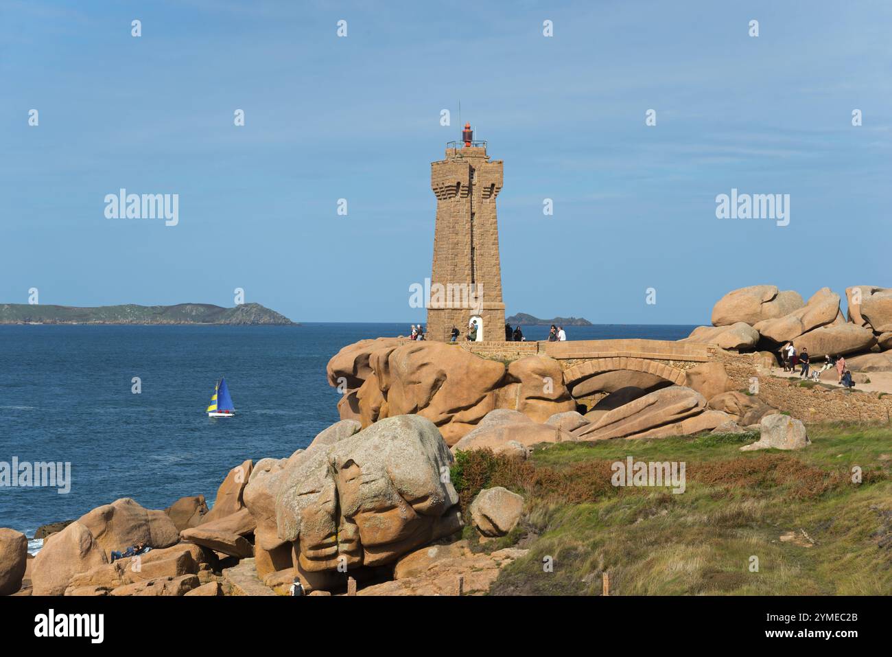 Lighthouse overlooking the rocky coast with sailing boat on the horizon ...
