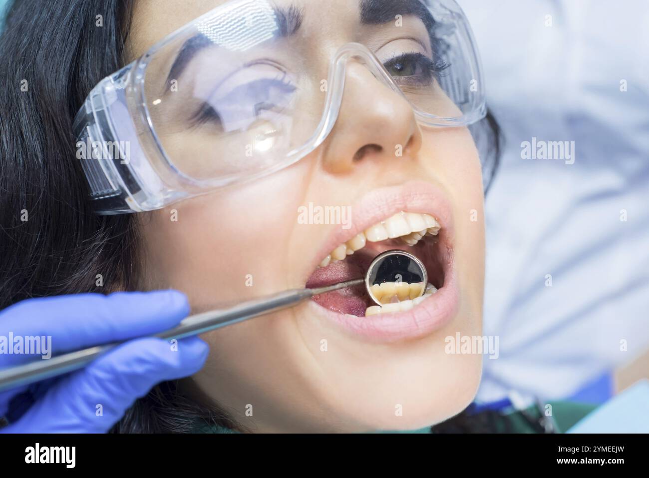 Stomatologist is using concave mirror. Female patient in safety glasses ...