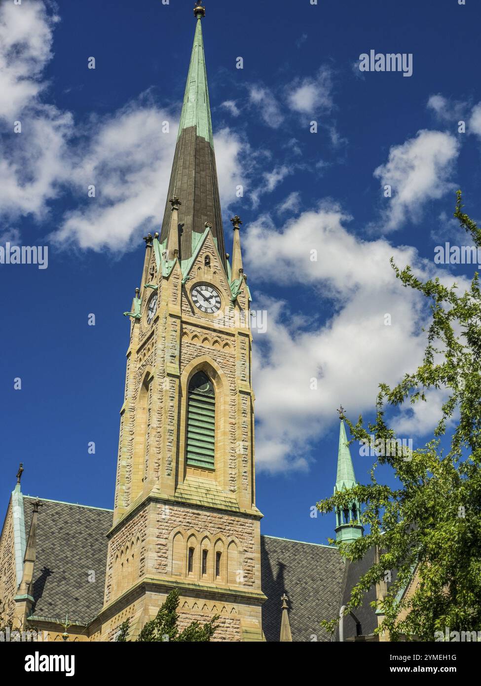 A gothic church tower with clock under a sky with white clouds ...