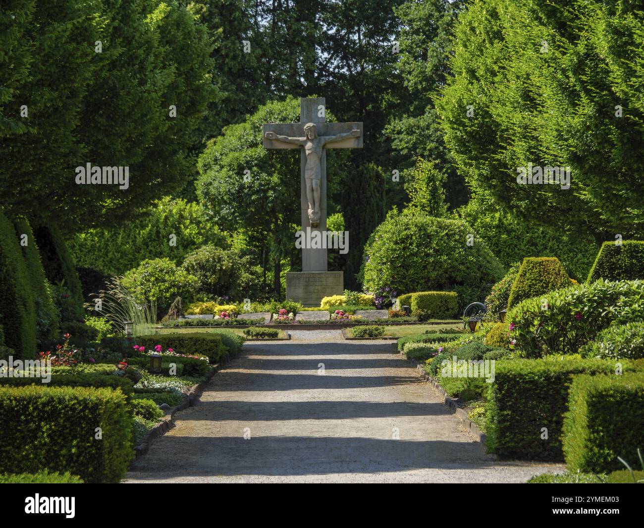 Cross with figure of Jesus along a shady cemetery path amidst green ...