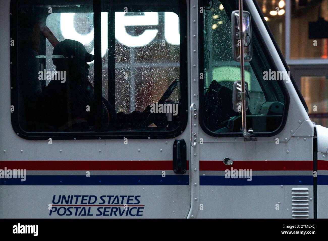 A United States Postal Service driver looks on as rain falls drives in ...