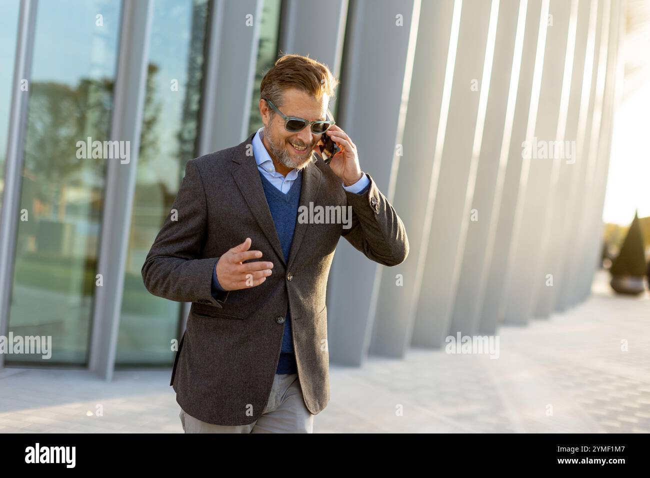 A well-dressed man enjoys a lively phone call while strolling beside a ...
