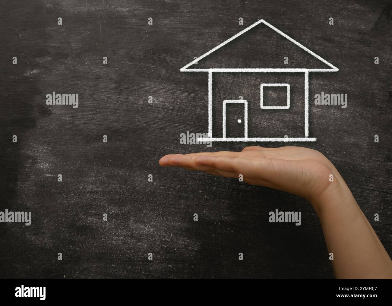 Hand holding a chalk drawing of a house. The drawing is on a blackboard ...