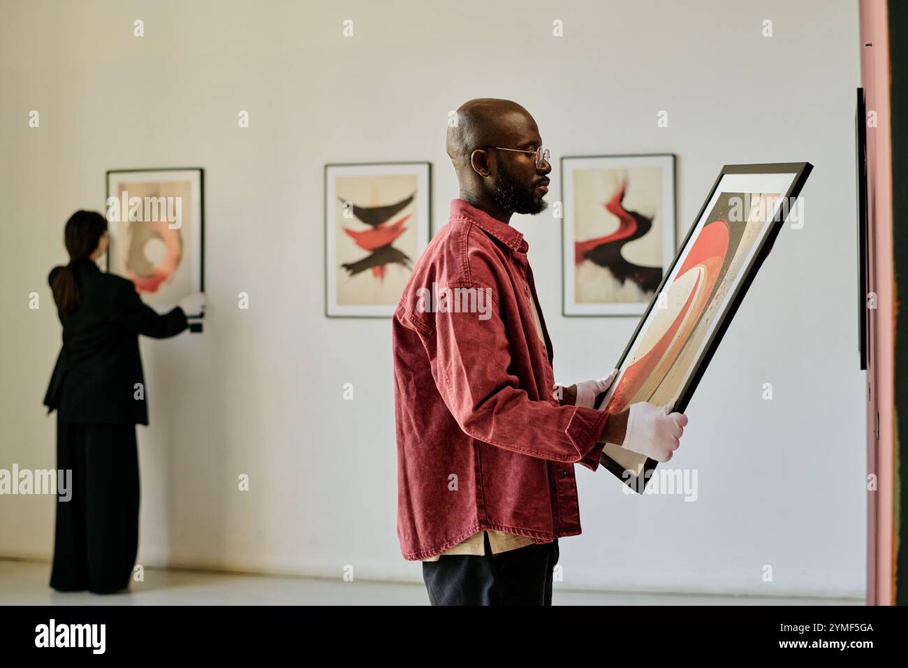 African American man holding abstract painting, curating art gallery ...