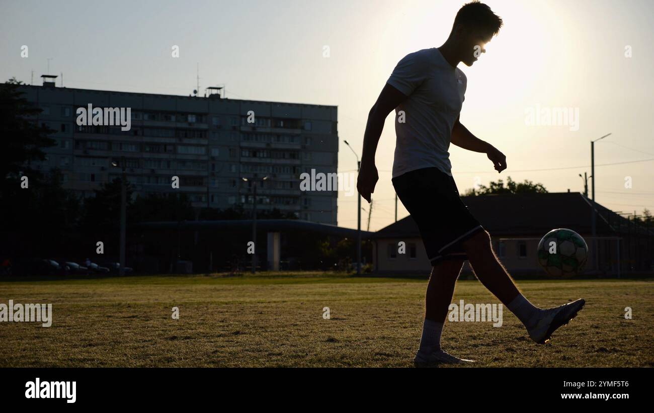 Professional footballer juggling soccer ball on stadium at sunset ...